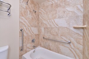 Casa de banho com banheira, azulejos de mármore e barras de apoio para acessibilidade.