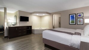 Quarto de hotel com uma cama grande, uma escrivaninha com cadeira, televisão de tela plana, banheira e quadros na parede.