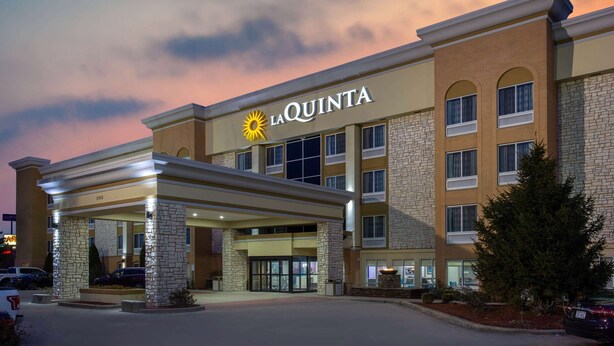Um hotel La Quinta com fachada de pedra, entrada coberta e estacionamento.