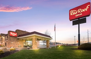 Um Red Roof Inn com fachada de tijolos, entrada coberta e gramado bem cuidado.
