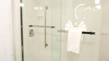 Chuveiro com divisória de vidro e toalha branca pendurada na maçaneta da porta.