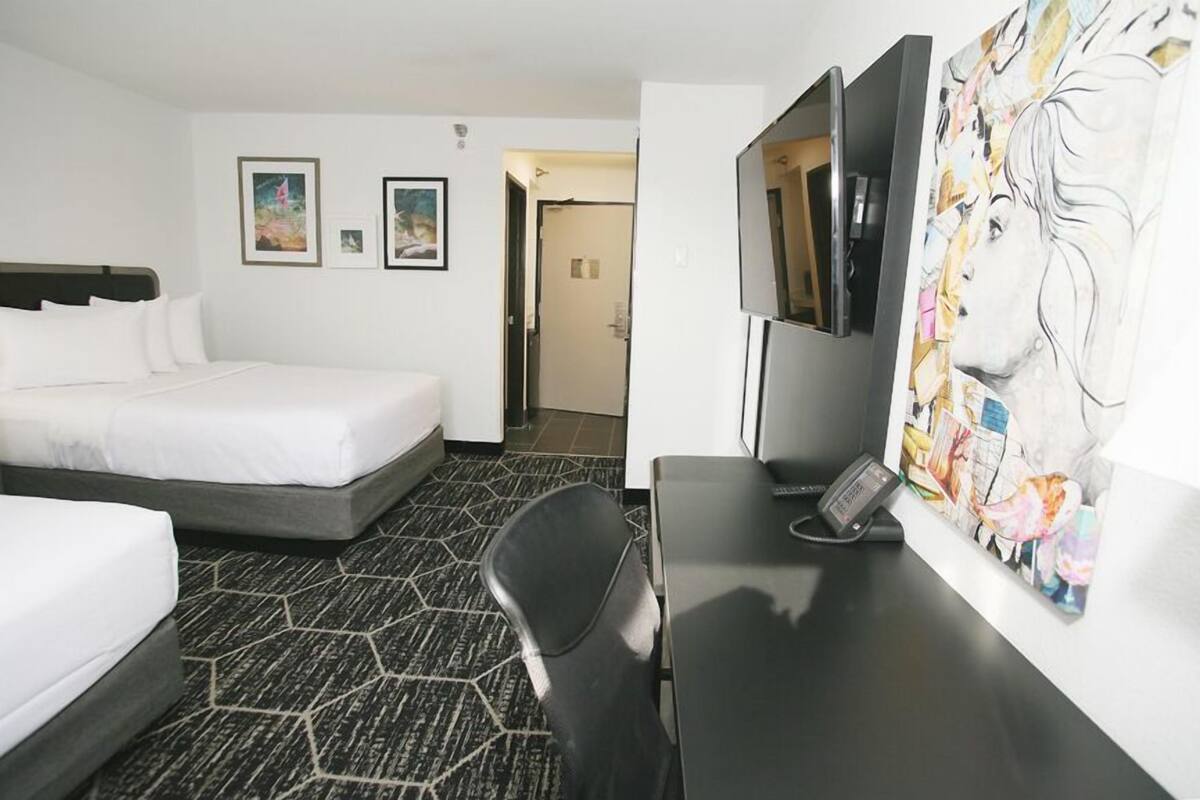 Quarto de hotel com cama, escrivaninha, cadeira, televisão e obras de arte na parede.