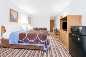 Quarto de hotel com cama, escrivaninha, televisão e frigorífico.
