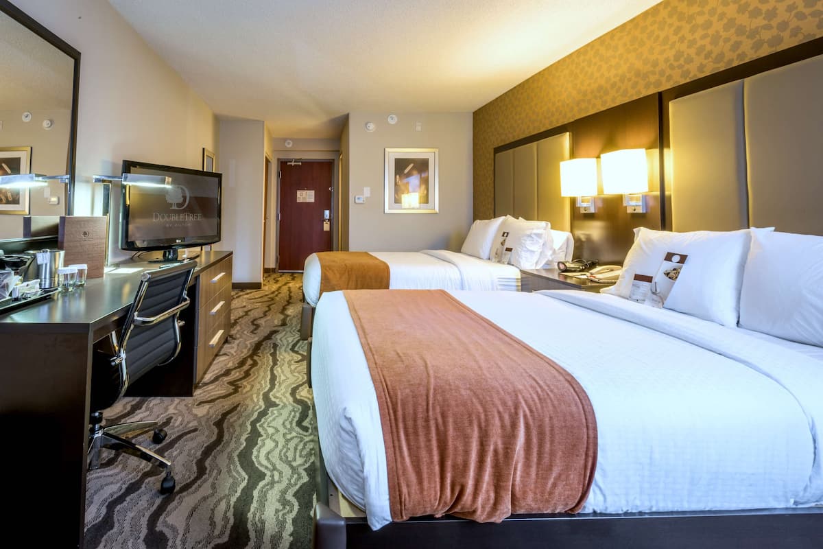 Quarto de hotel com cama, escrivaninha com computador, televisão e porta do banheiro.