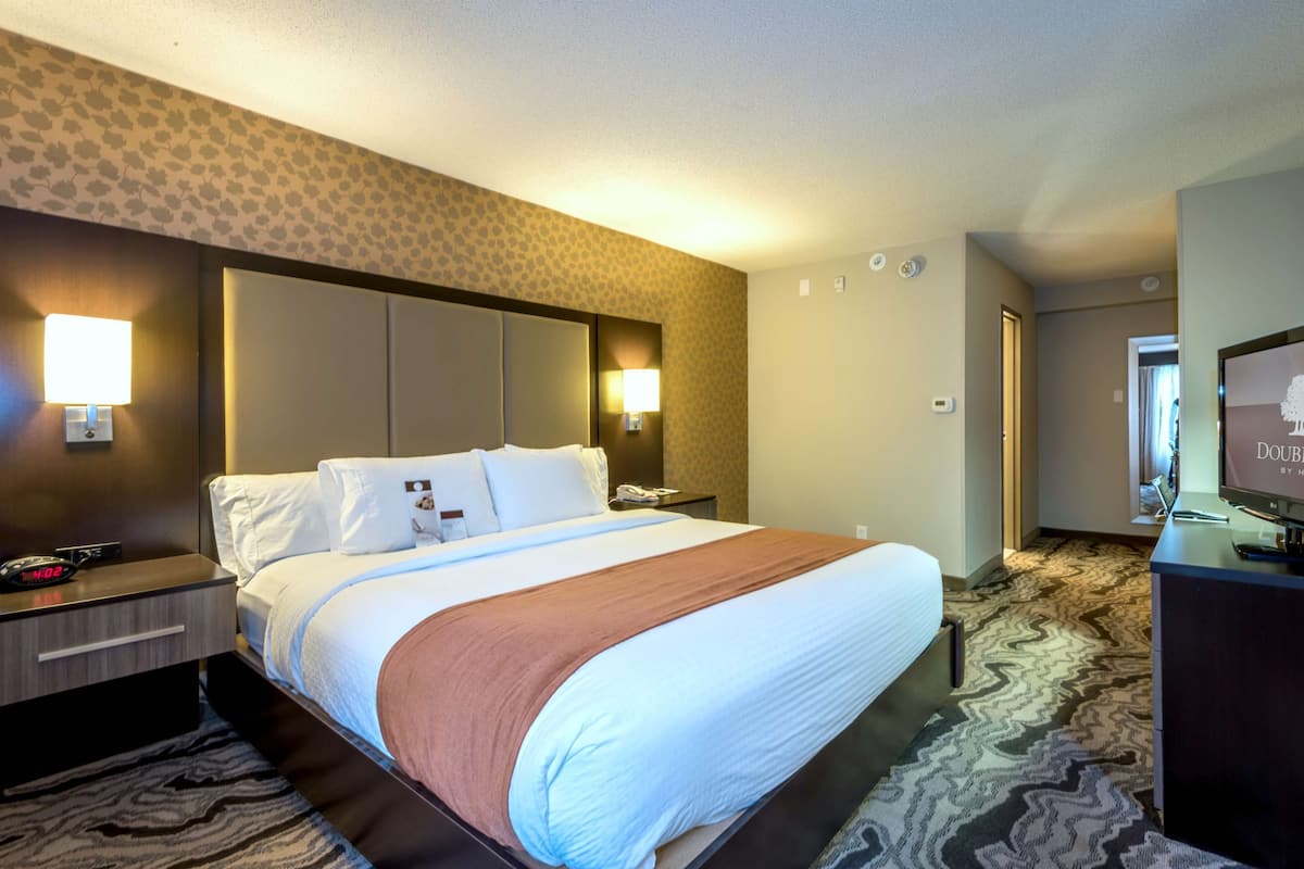 Quarto de hotel com cama grande, mesa de cabeceira, escrivaninha e televisão.