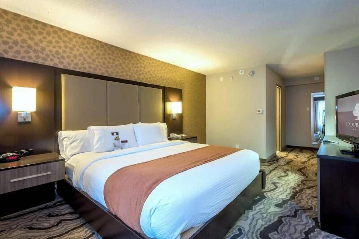 Quarto de hotel com uma cama grande, abajures, escrivaninha e televisão.
