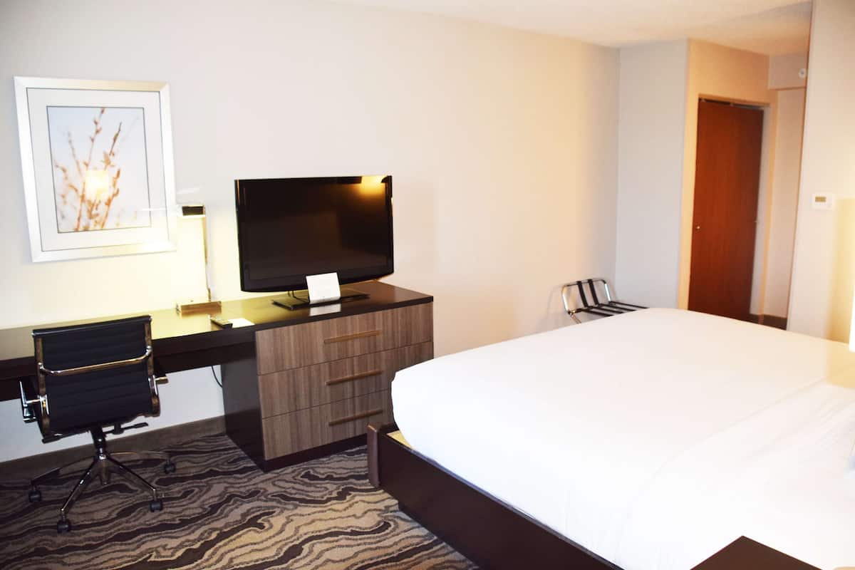 Quarto de hotel com cama, escrivaninha com computador, televisão e cadeira.
