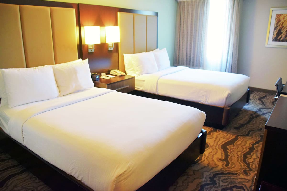 Quarto de hotel com duas camas, uma mesa de cabeceira com telefone e uma luminária.