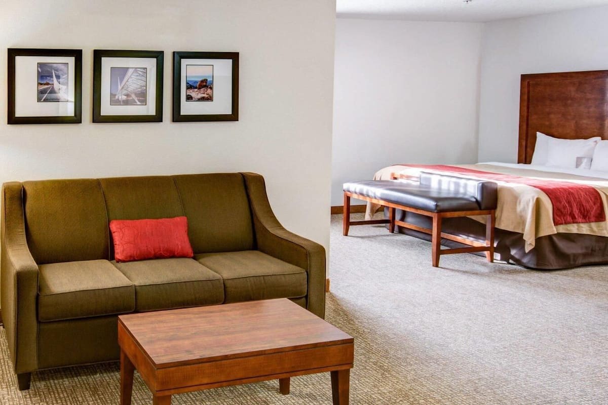 Quarto com sofá, mesa de madeira, cama com cabeceira e três quadros na parede.