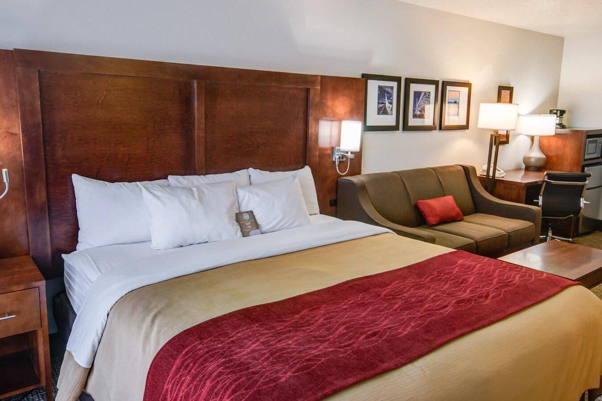 Quarto de hotel com uma cama grande, um sofá, uma escrivaninha e uma luminária.