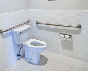 Casa de banho com paredes azulejadas em branco, sanita branca e barras de apoio para segurança.