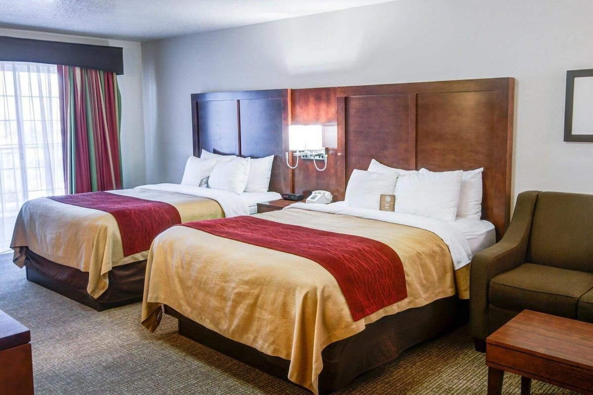 Quarto de hotel com duas camas, um sofá, uma mesinha e uma mesa de cabeceira.