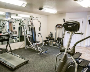Uma academia com equipamentos de cardio, aparelhos de musculação e um espelho.