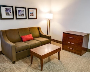 Quarto com sofá, mesa de madeira, cômoda e três quadros na parede.