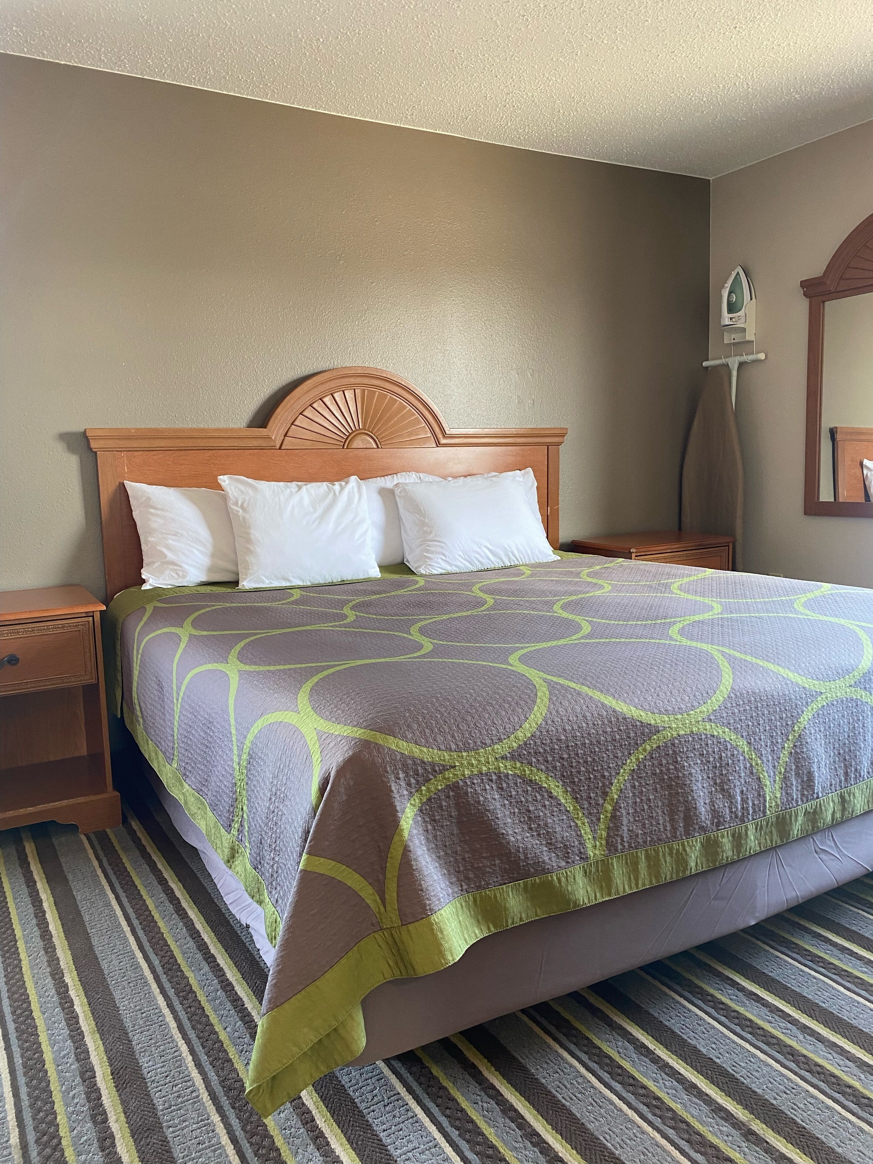 Uma cama bem arrumada com colcha estampada, cabeceira de madeira e mesa de cabeceira com abajur.