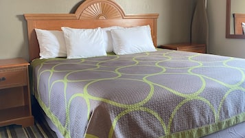 Uma cama bem arrumada com colcha estampada, cabeceira de madeira e mesa de cabeceira com abajur.