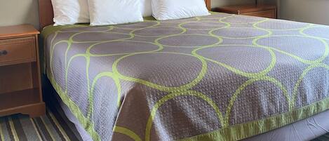 Uma cama bem arrumada com colcha estampada, cabeceira de madeira e mesa de cabeceira com abajur.