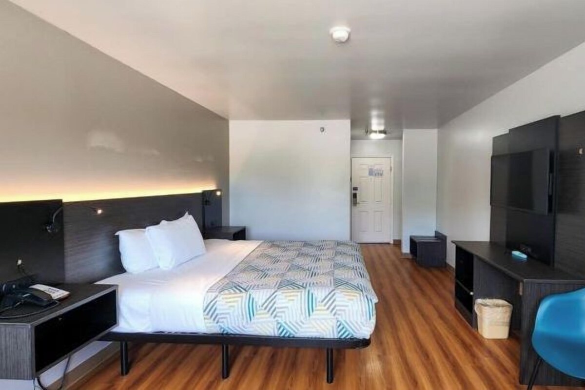 Quarto de hotel com cama, mesas de cabeceira, televisão, poltrona e porta.