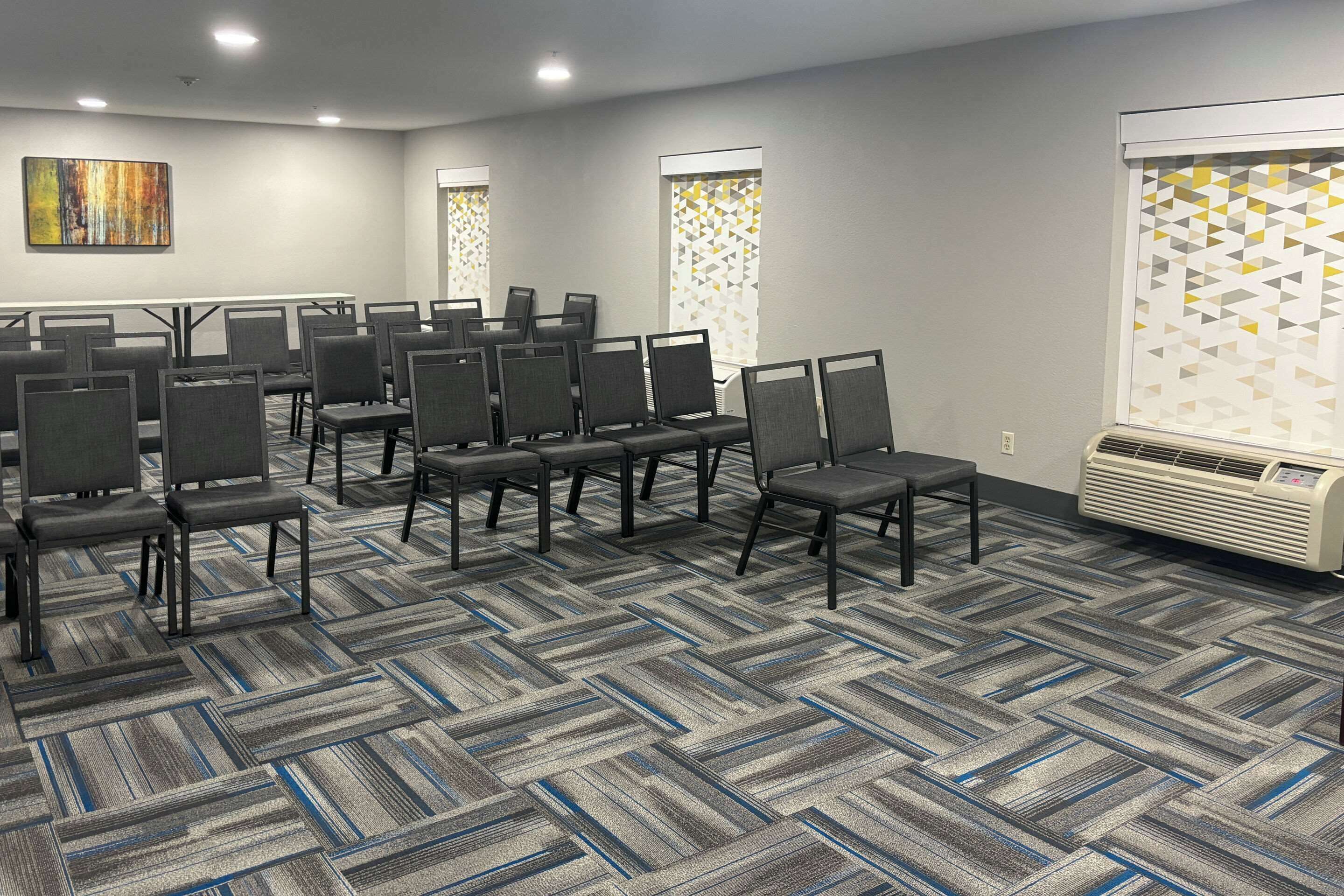 Uma sala de conferências com fileiras de cadeiras, piso coberto por carpete e um aparelho de ar condicionado grande.