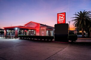 Um Red Roof Inn com letreiro de neon vermelho, fachada de tijolos e estacionamento.