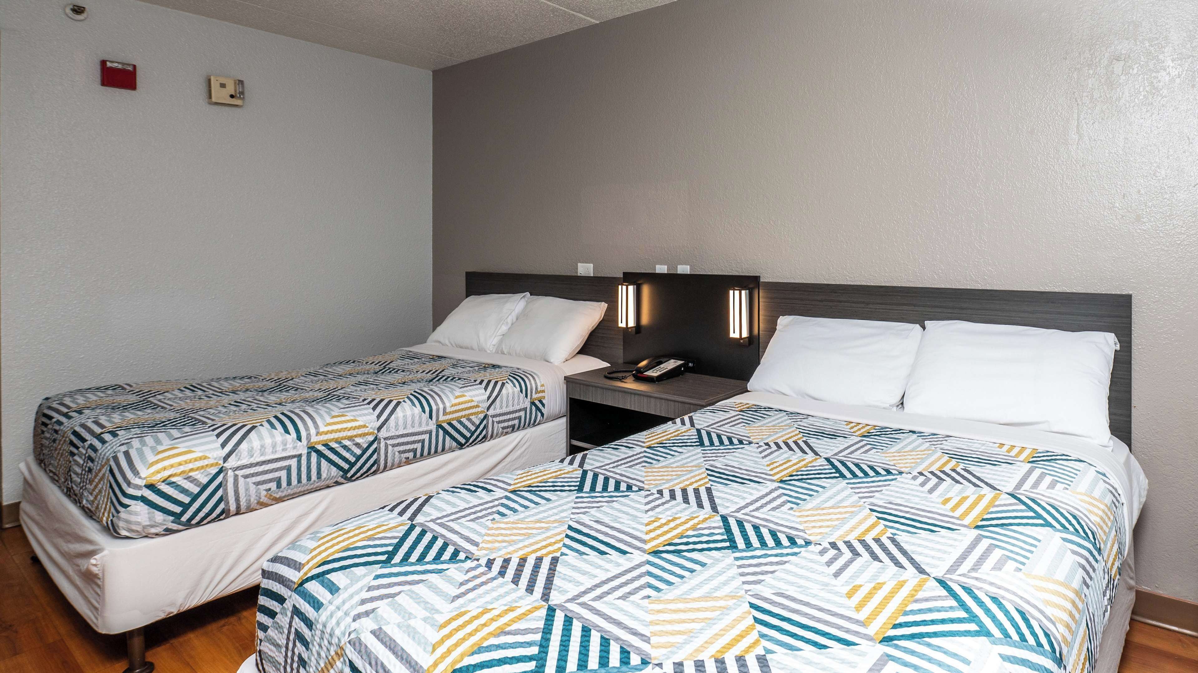 Quarto de hotel com duas camas de solteiro, cada uma com roupa de cama estampada, mesa de cabeceira com telefone e luminária na parede.
