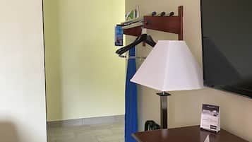 Quarto de hotel com cômoda de madeira, luminária branca, cortina azul e televisão fixada na parede.