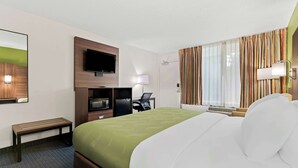 Quarto de hotel com uma cama grande, uma escrivaninha com cadeira, televisão fixada na parede e uma janela com cortinas.