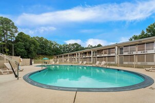 Piscina com espreguiçadeiras e um edifício com varandas ao fundo.