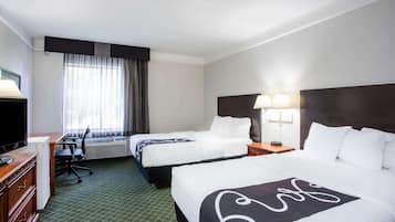 Quarto de hotel com duas camas, uma mesa, televisão e janela com cortinas.