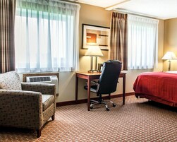 Quarto de hotel com uma cama, uma escrivaninha, uma cadeira e uma janela com cortinas.
