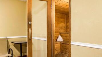 Uma porta de madeira dá acesso a um espaço sauna com um banco de madeira e uma pilha de toalhas.