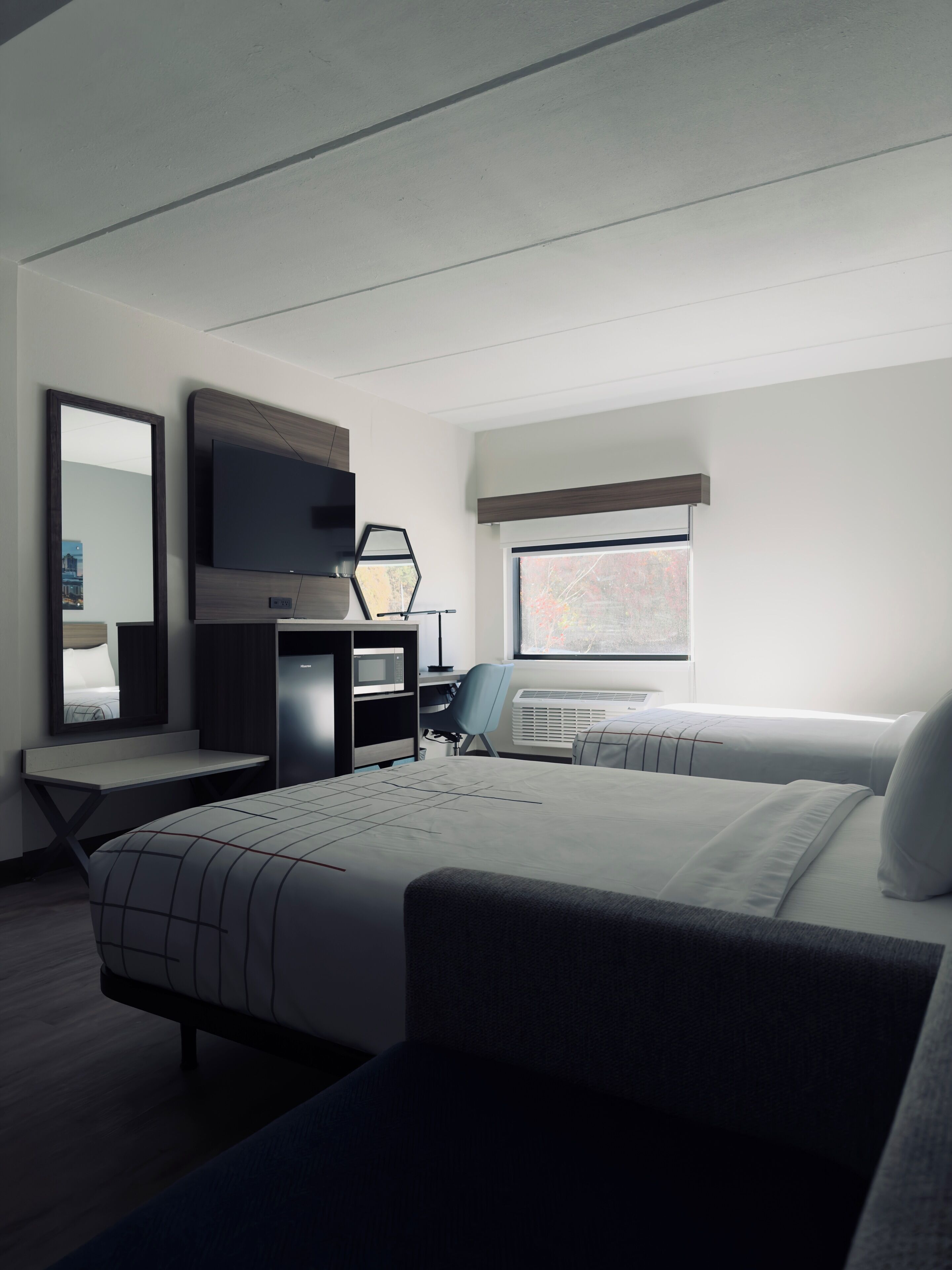 Quarto de hotel moderno com uma cama grande, uma escrivaninha com computador, televisão de tela plana e janela com vista para árvores.