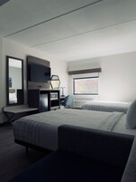 Quarto de hotel moderno com uma cama grande, uma escrivaninha com computador, televisão de tela plana e janela com vista para árvores.