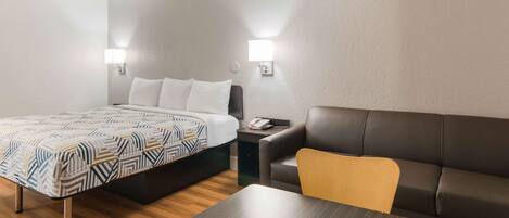 Quarto de hotel com cama, mesa de cabeceira, luminária, sofá e mesa.