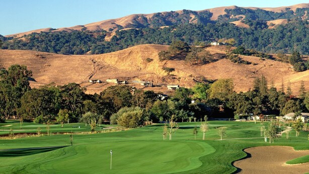 Um campo de golfe com um clube, rodeado por colinas e árvores.