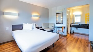 Quarto de hotel com cama, mesa de cabeceira, cadeira e banheiro com pia e espelho.