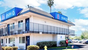 Um motel com estrutura em dois andares, varanda no segundo andar e estacionamento com carros.
