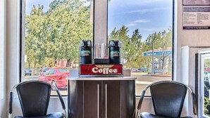 Estação de café com duas cadeiras e vista para um carro vermelho e árvores lá fora.