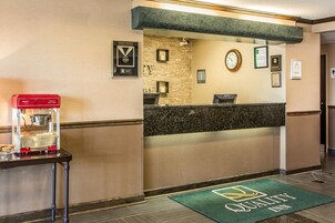 Uma área de recepção de hotel com uma máquina de café, um relógio e diversas premiações na parede.
