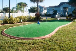 Um campo de mini golfe com superfície verde, duas bandeiras e uma borda vermelha.