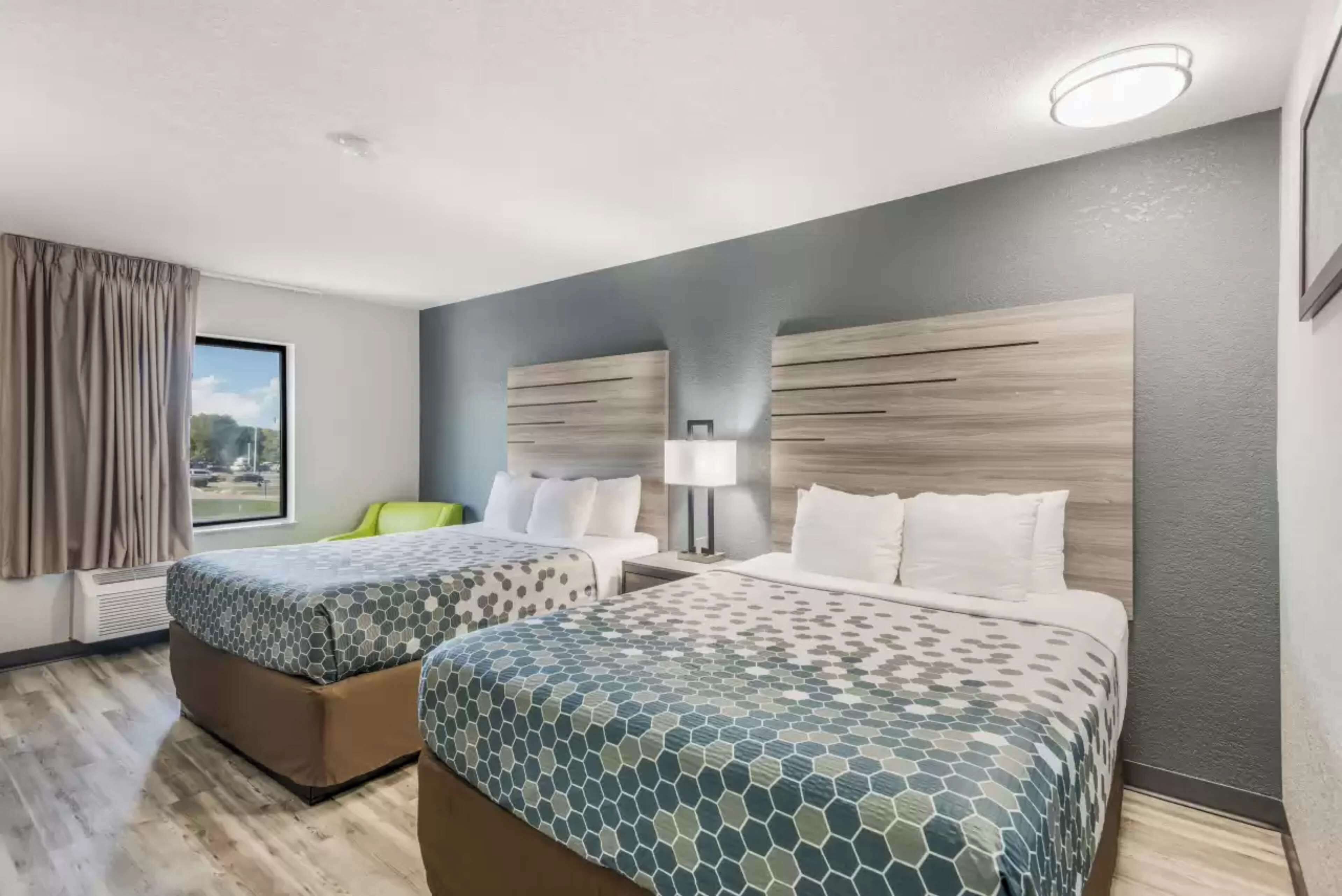 Quarto de hotel com duas camas, janela com cortinas, vista para o exterior e design moderno com parede cinza e cabeceira de madeira.
