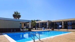 Piscina com escadas de metal, uma palmeira e um edifício com uma placa que diz 'AVISO'.
