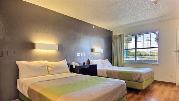 Quarto de hotel com duas camas, janela com cortinas, mesa de cabeceira com telefone e luminária fixada na parede.