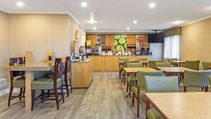 Um restaurante com balcão, banquetas no bar e várias mesas com cadeiras.