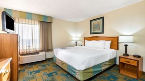 Quarto de hotel com cama, abajures, televisão, aquecedor e janela com cortinas.