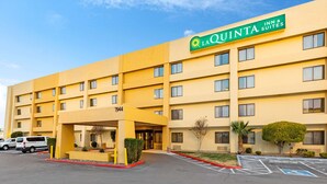 Um hotel de vários andares com fachada amarela, uma placa de destaque com a inscrição "LA QUINTA INN & SUITES" e um estacionamento com vagas para deficientes.