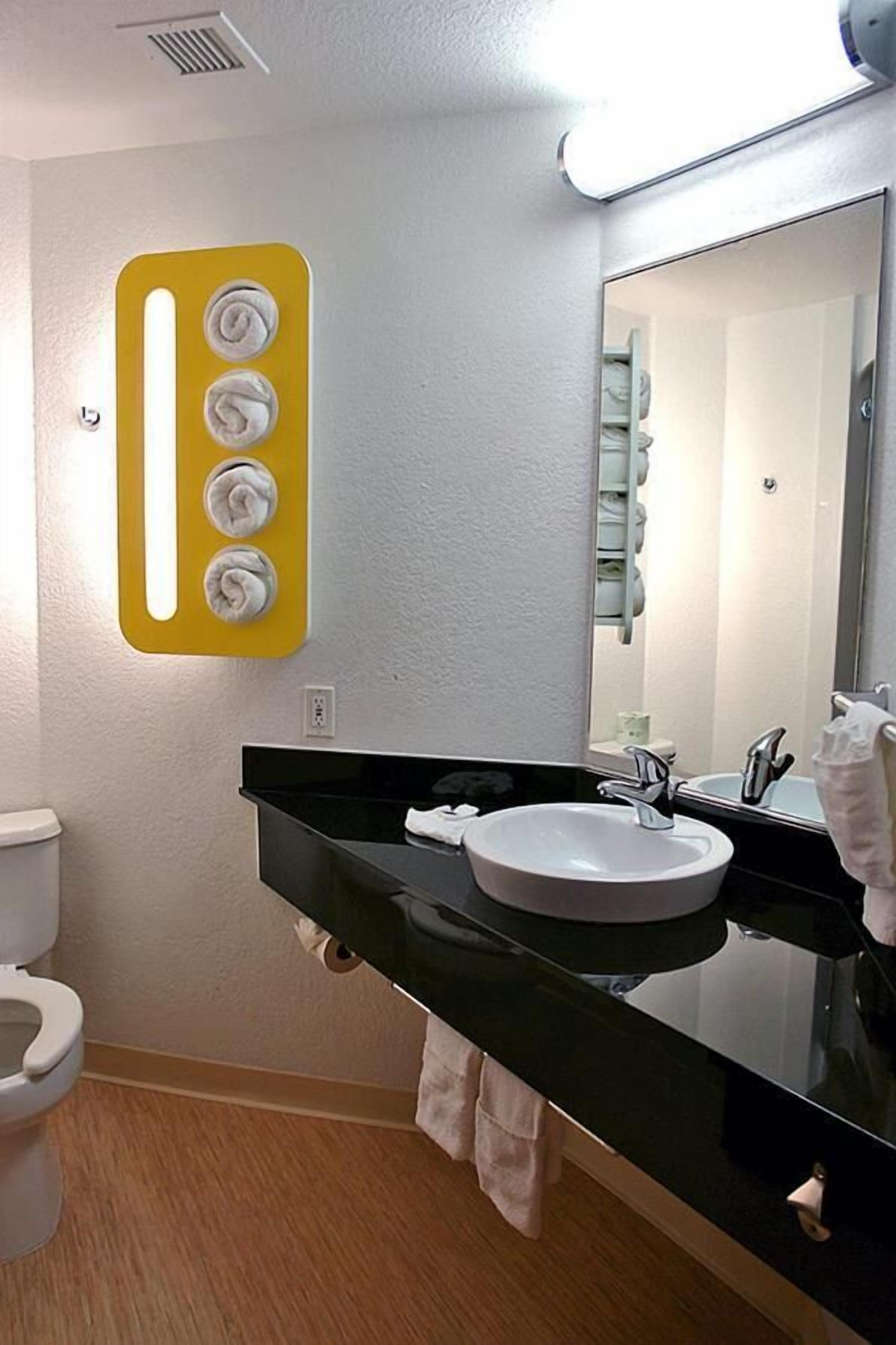 Casa de banho com sanita branca, lavatório preto, espelho e toalheiro amarelo com quatro toalhas.