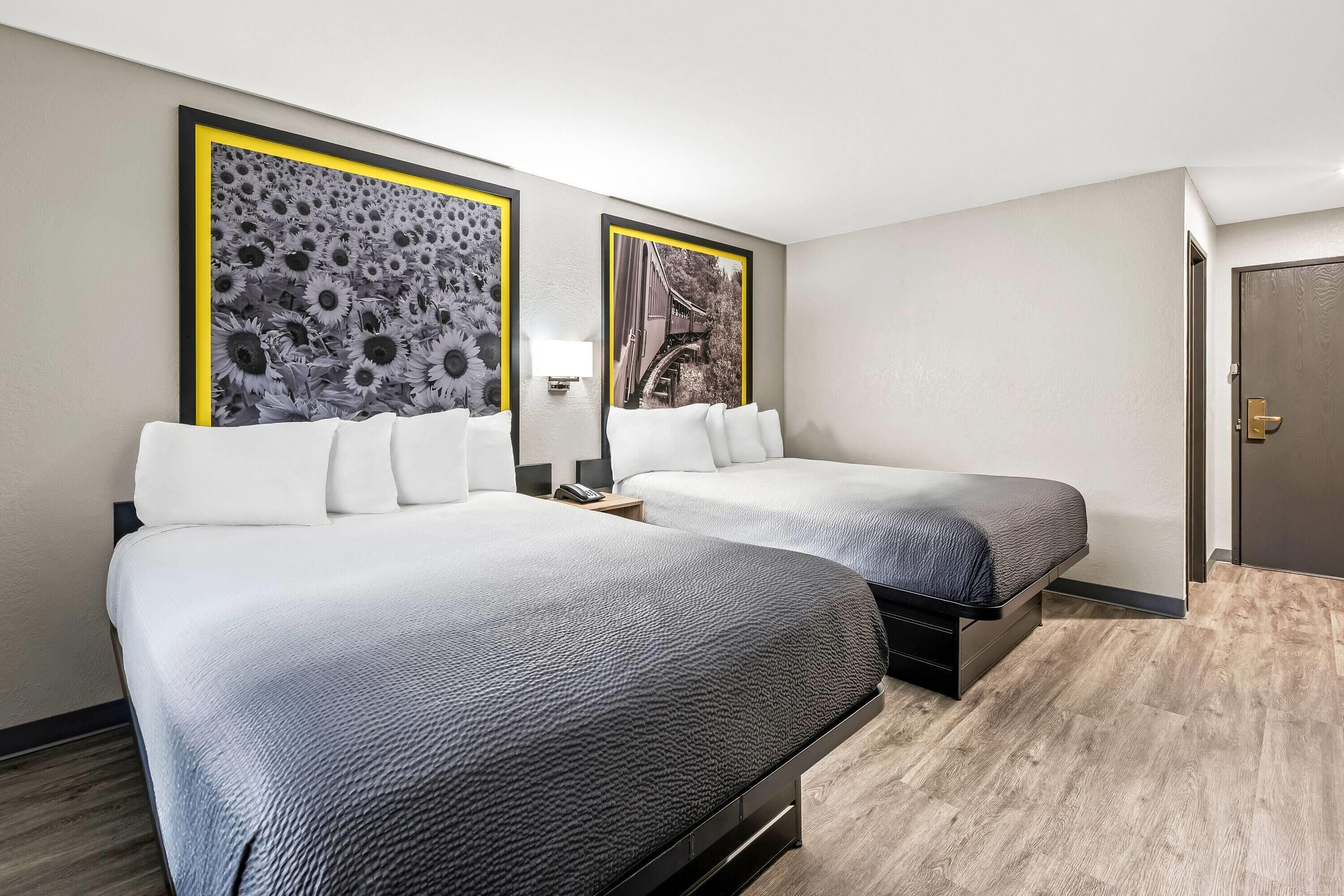 Quarto de hotel com duas camas, piso de madeira e duas grandes molduras na parede.