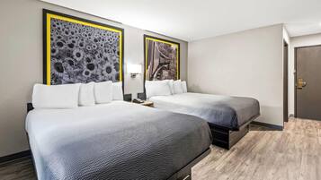Quarto de hotel com duas camas, piso de madeira e duas grandes molduras na parede.
