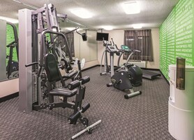 Uma academia com diversos equipamentos de exercício, uma televisão e uma parede verde com mensagens motivacionais.